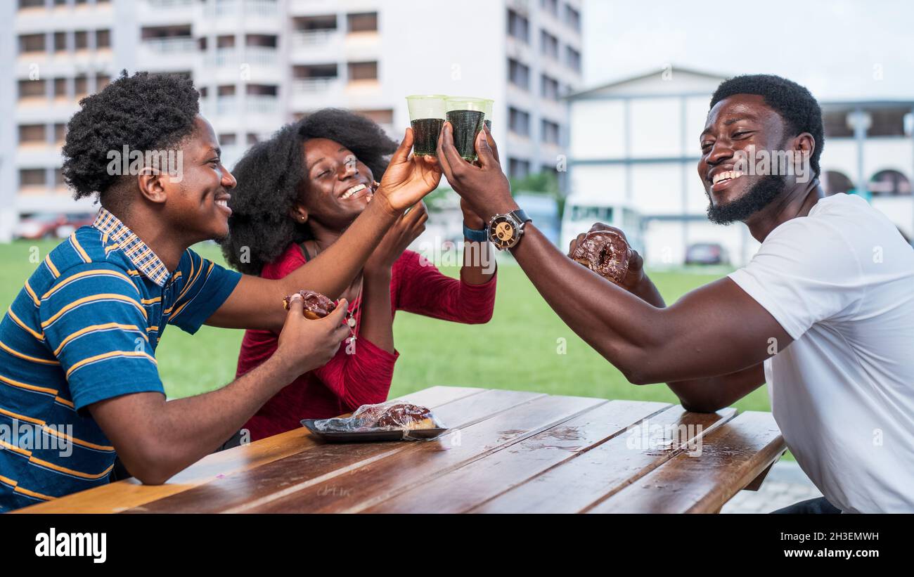 Group of African friends laughing and eating donuts outdoors Stock ...