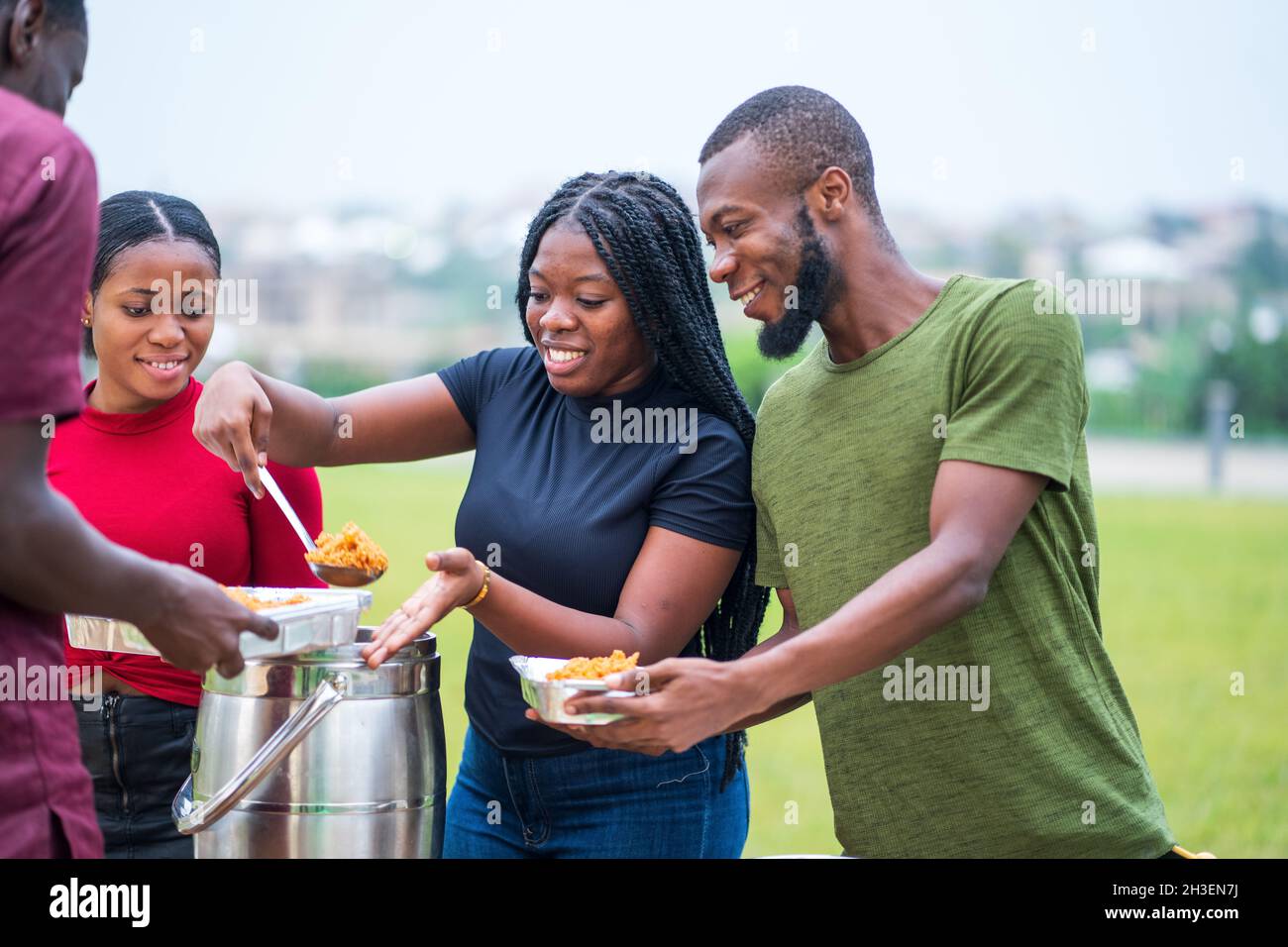 Smiling African female providing food to a group of people outdoors ...