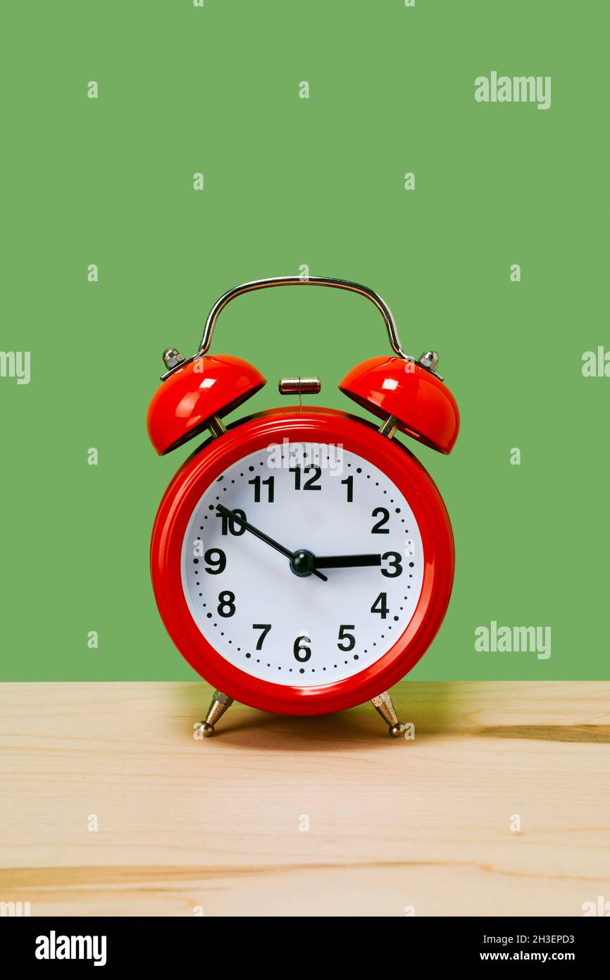 closeup of a traditional red alarm clock, set at ten to three, on a ...