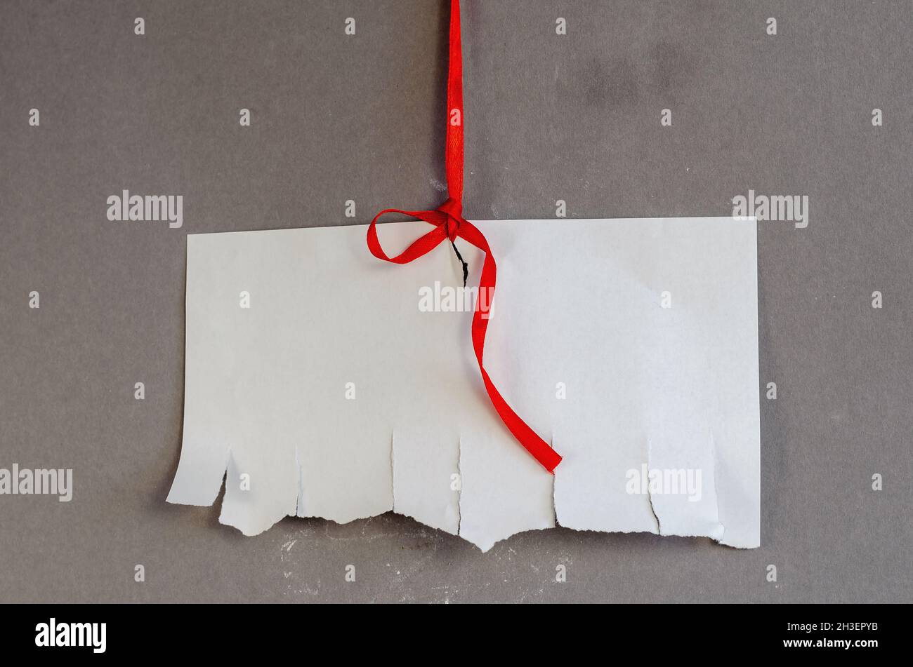 White sheet of paper with tear-off pieces and red ribbon against a gray ...