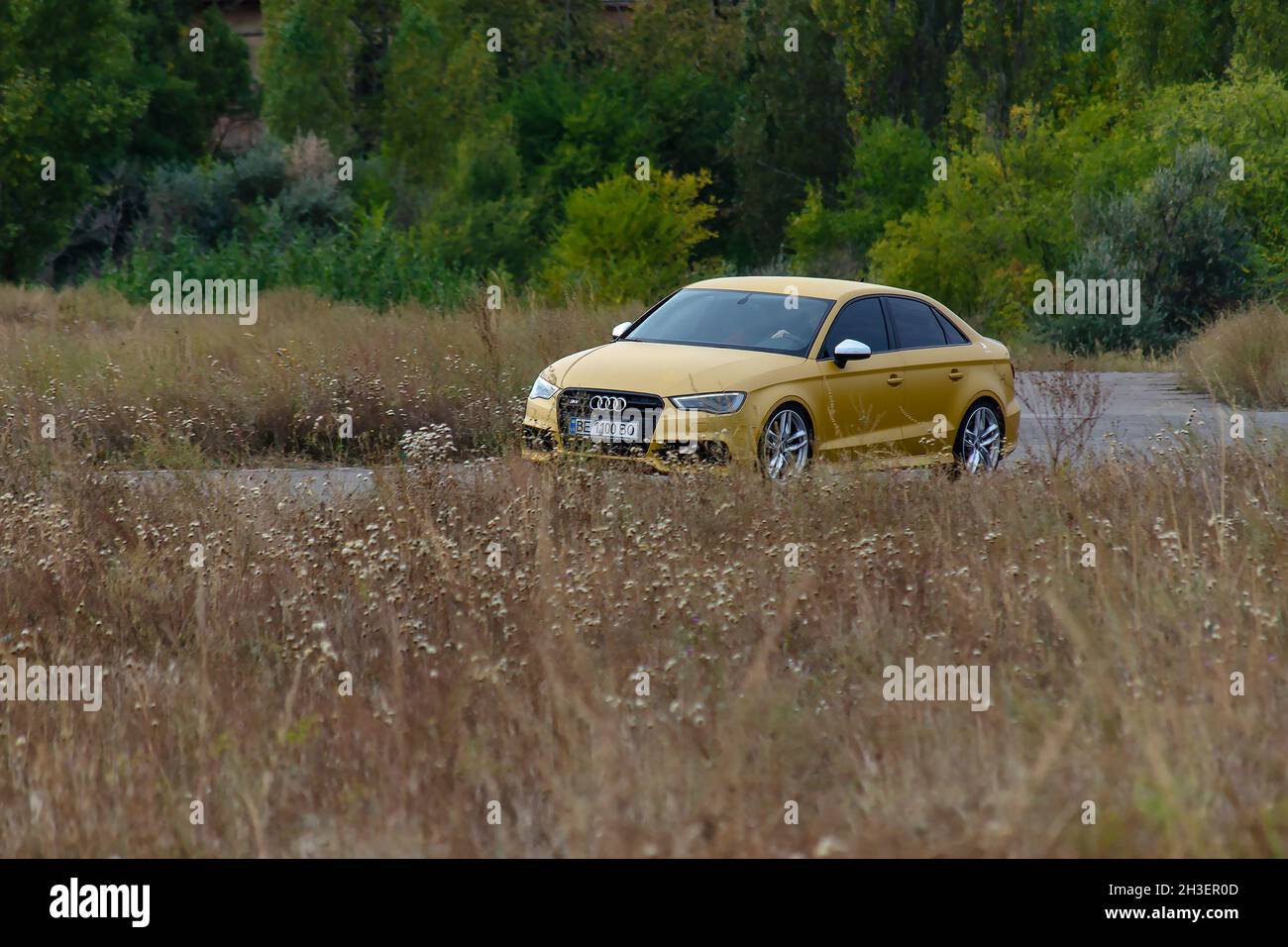 A sporty yellow sedan drives at high speed on an autumn paved road ...