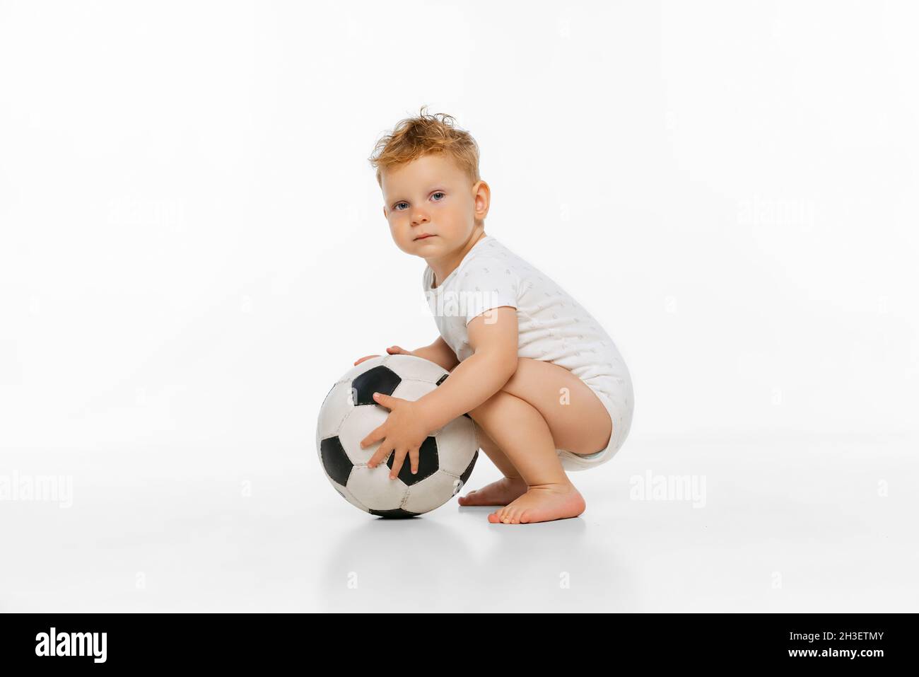 Full-length portrait of little boy, child in bodysuit playing with ...