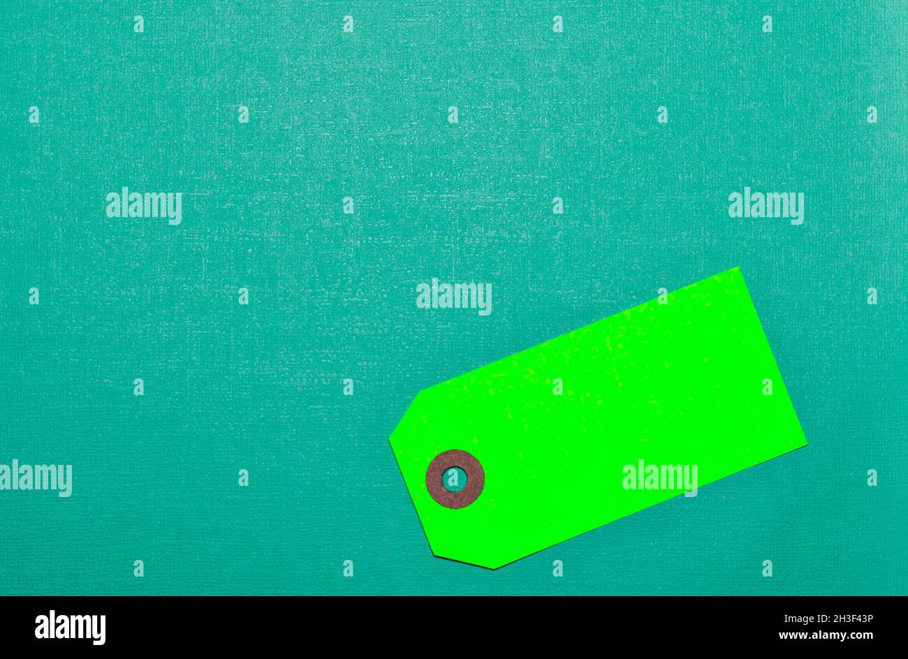 Green blank label tag on a teal cardstock background with copy space ...