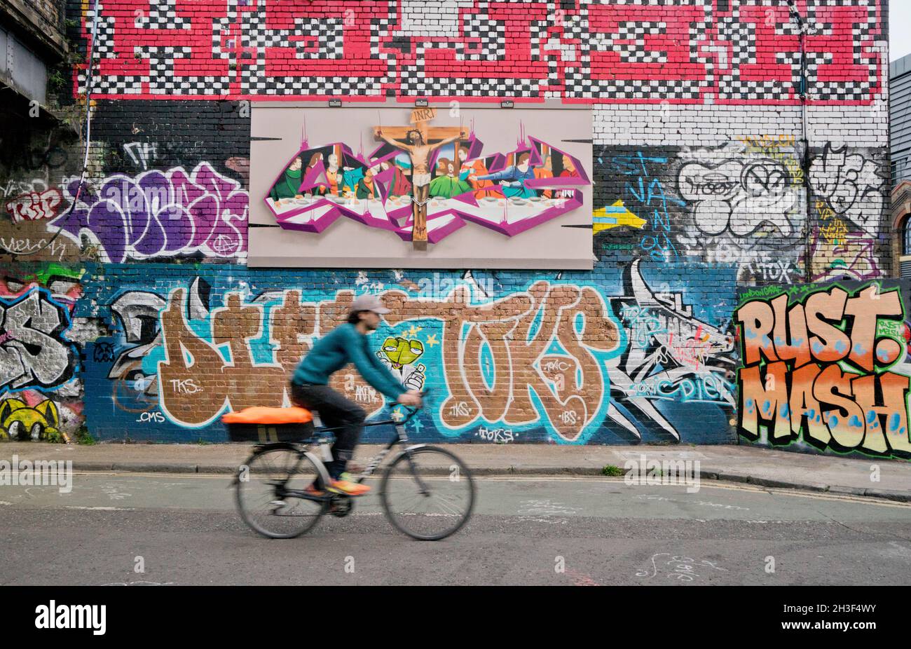 People walking and cycling past a train bridge with graffiti in ...