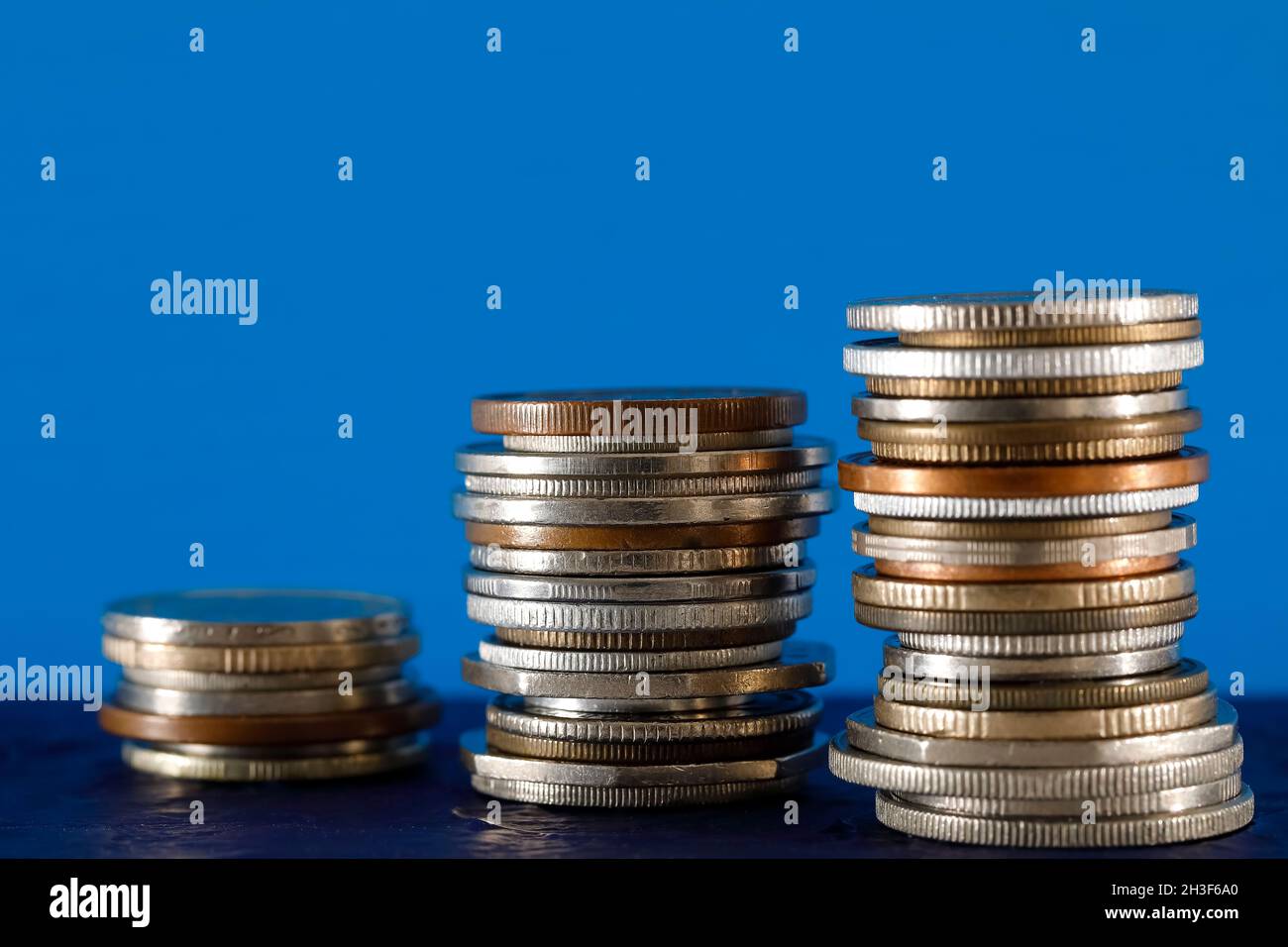 Three piles of various coins is visible on blue background. The surface ...