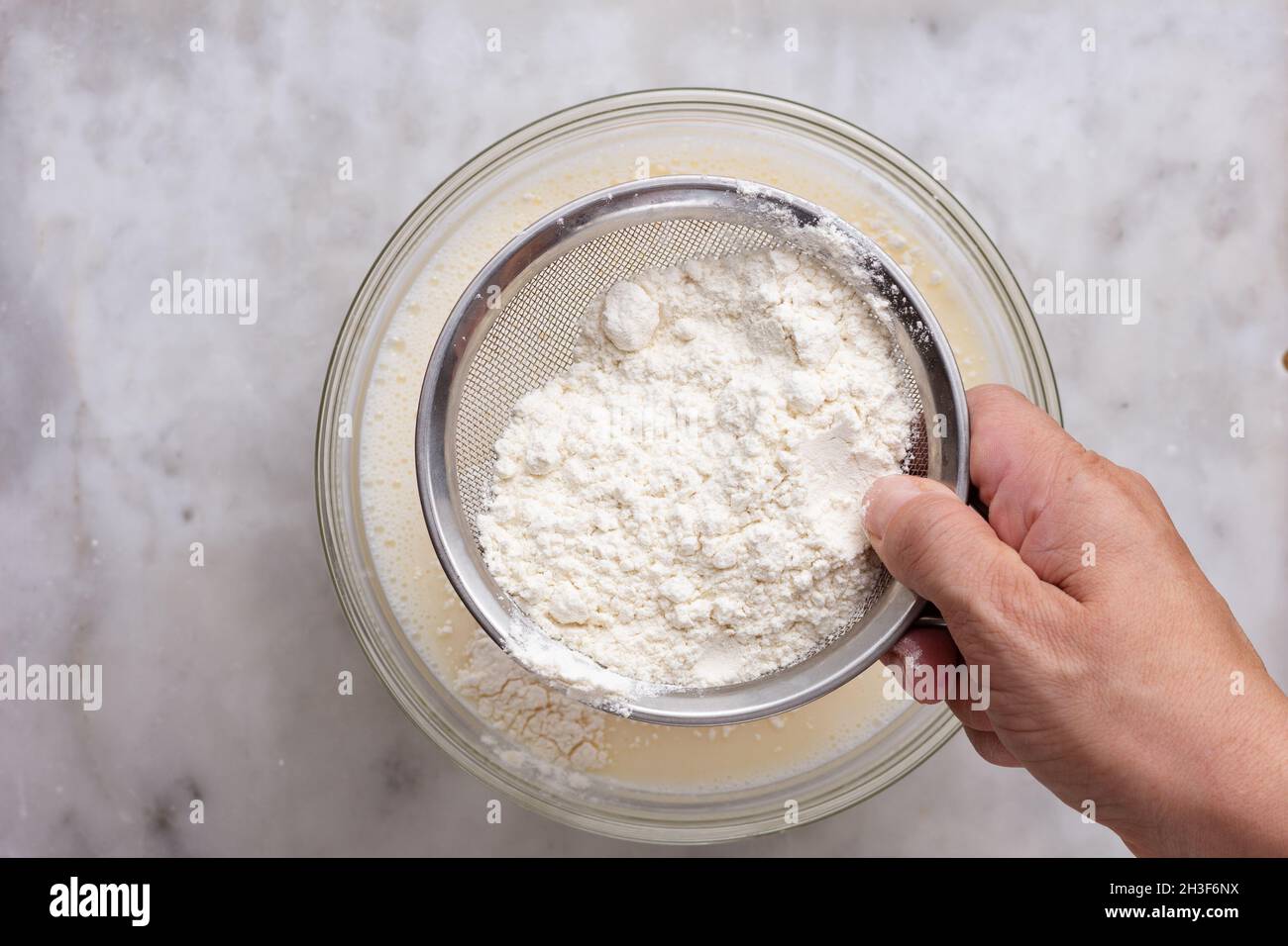 Top view of woman hand holding sieve with flour and sifting into batter ...