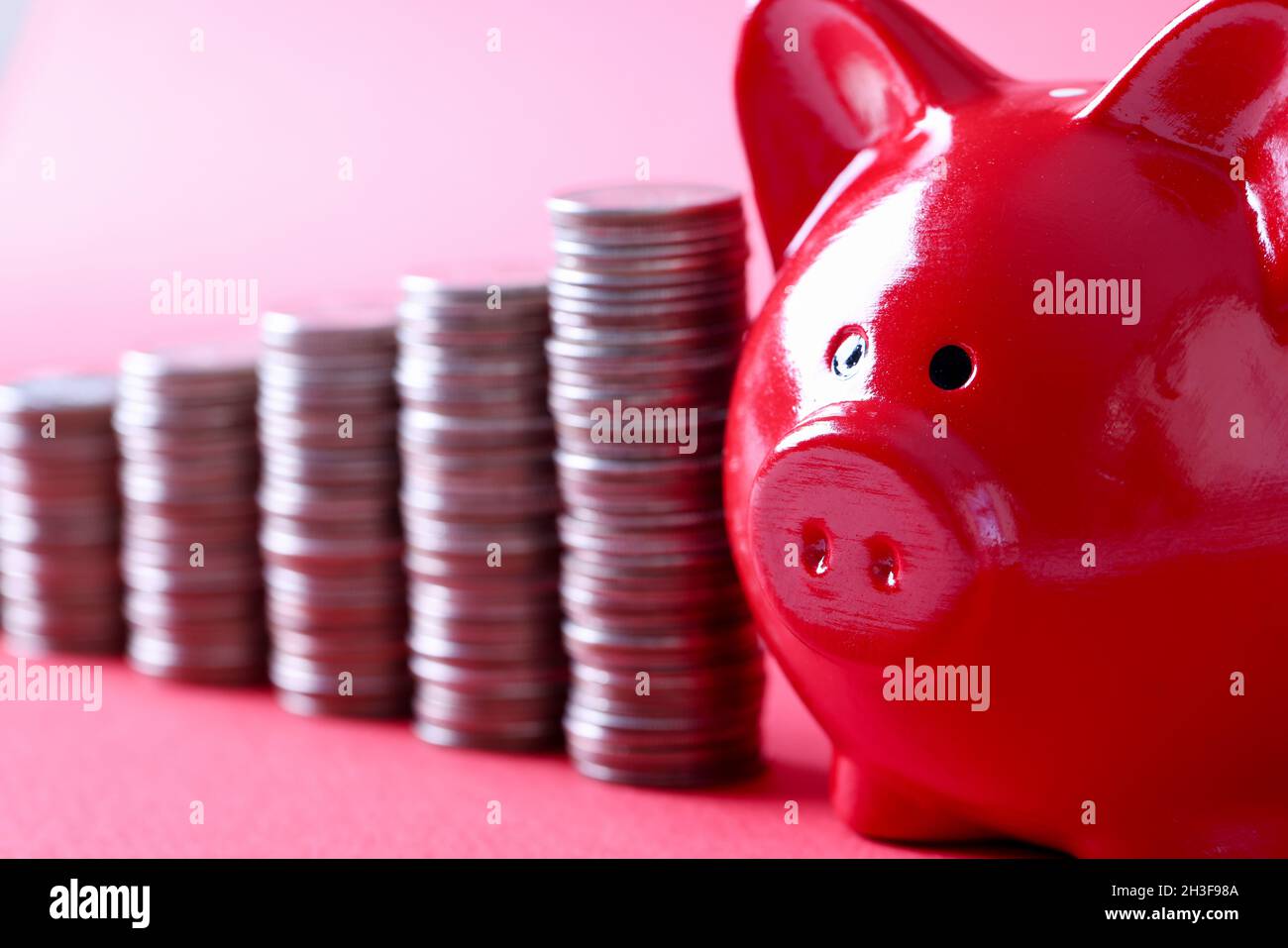 Red piggy bank standing near heaps of coins in ascending order closeup ...