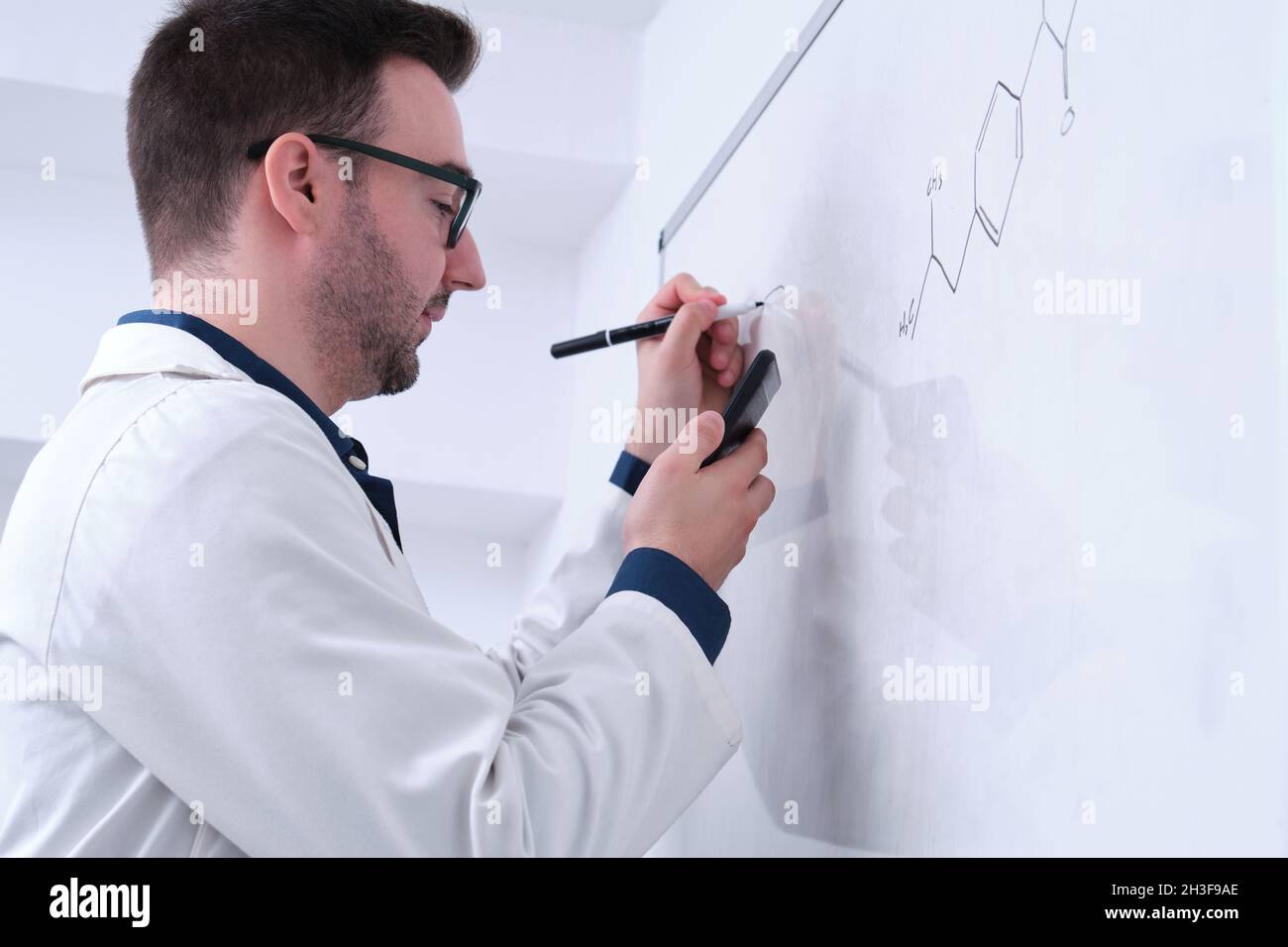 Male researcher in lab coat writing notes on whiteboard Stock Photo - Alamy