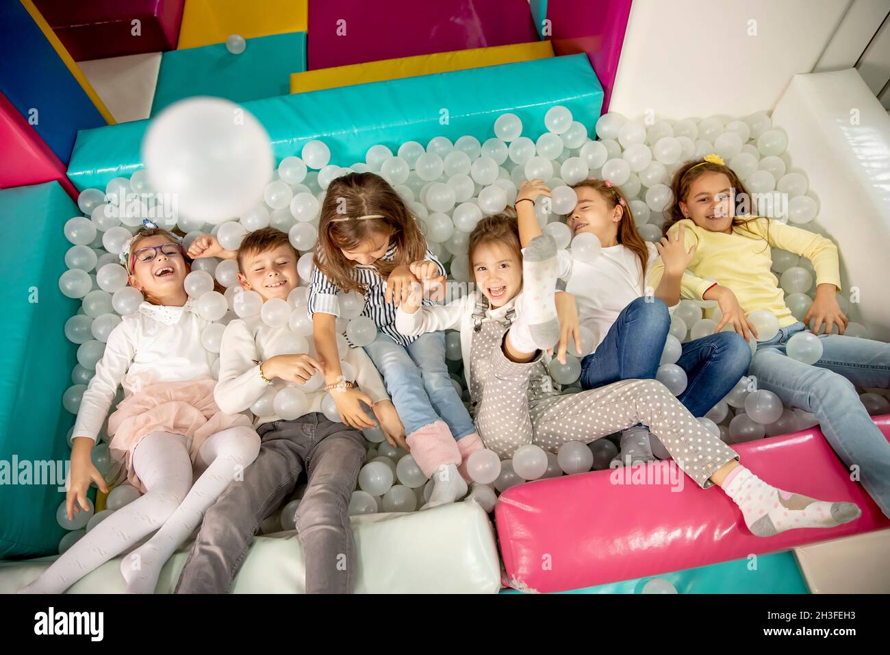 Group of happy little kids in ball pit smiling happily at camera while ...