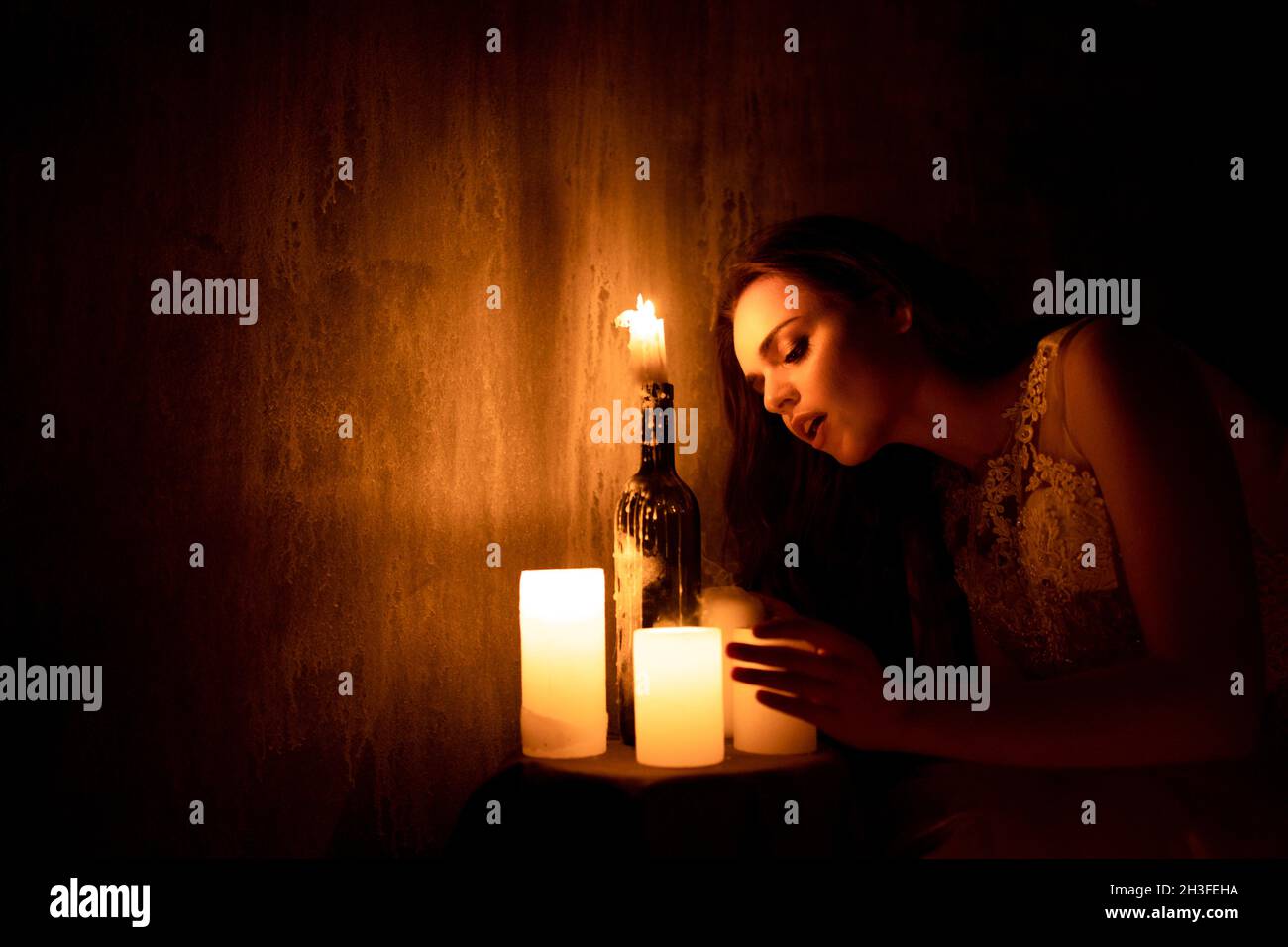 A woman is sitting in a room by candlelight. A young girl looks at ...