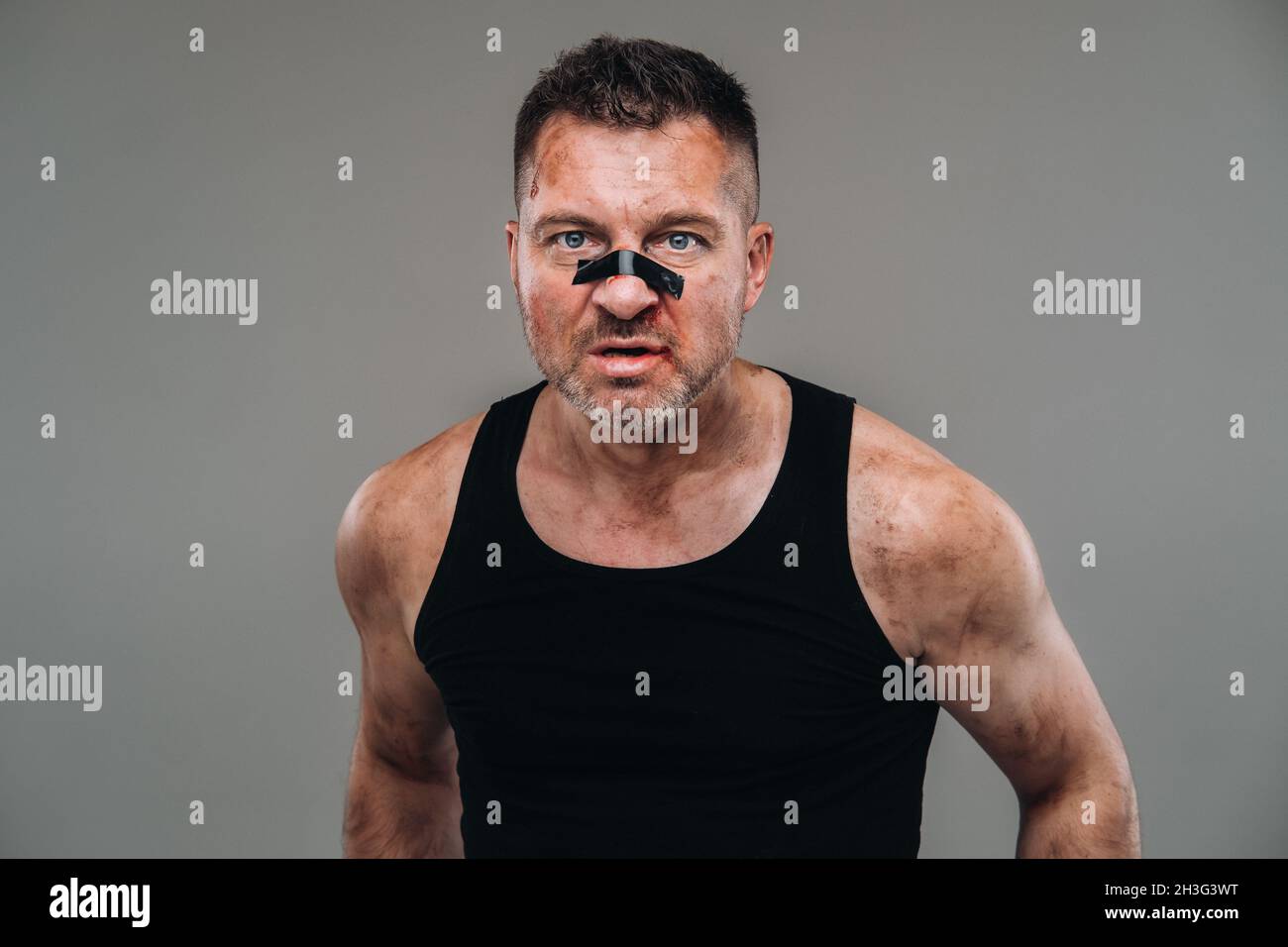 on a gray background stands a battered man in a black T shirt looking ...