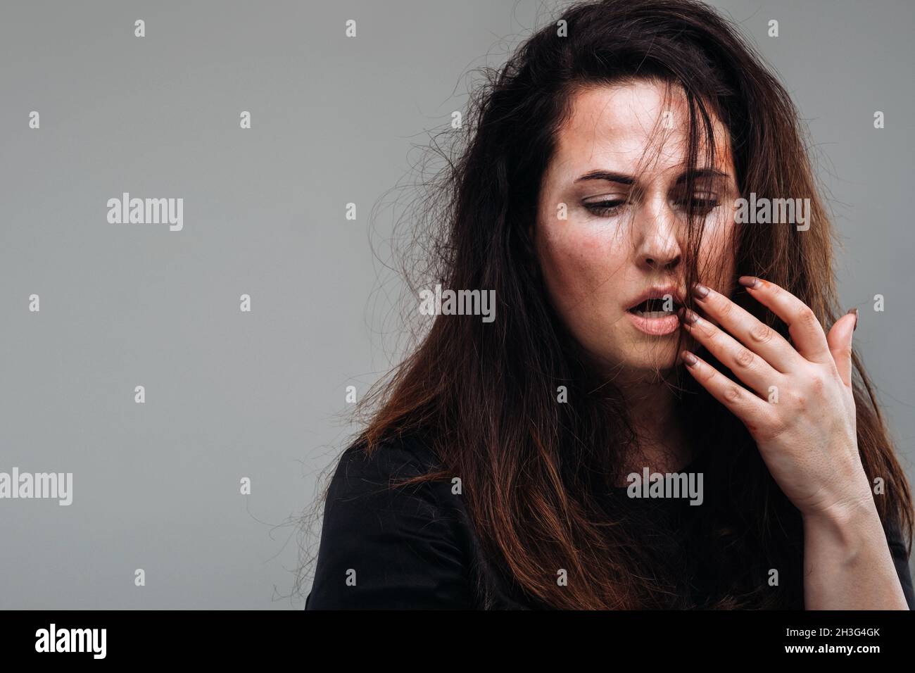 a battered woman in black clothes on an isolated gray background ...
