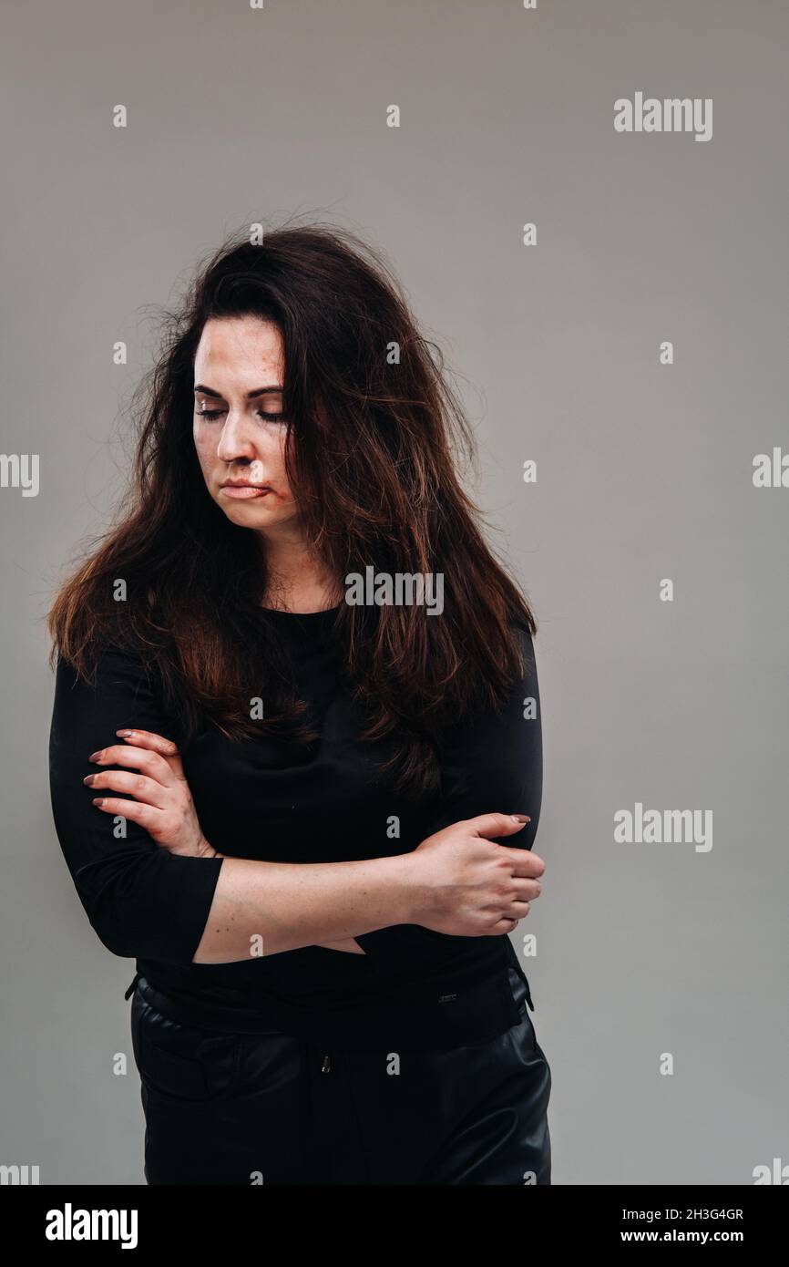 a battered woman in black clothes on an isolated gray background ...