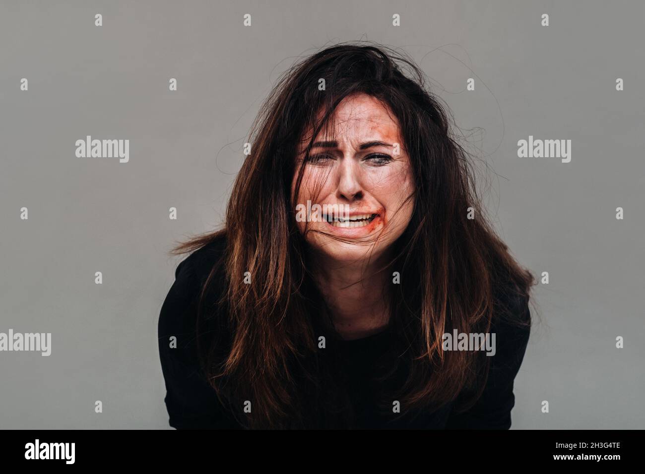 a battered woman in black clothes on an isolated gray background ...