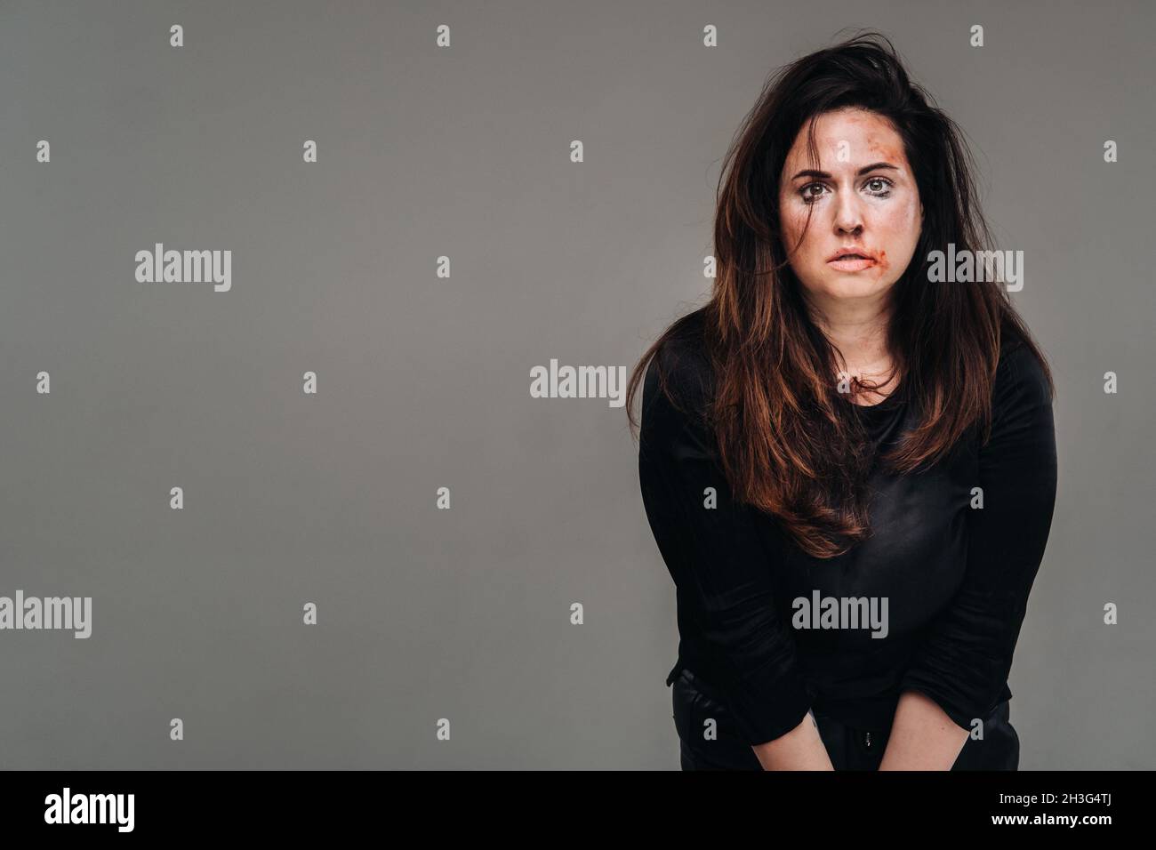 a battered woman in black clothes on an isolated gray background ...