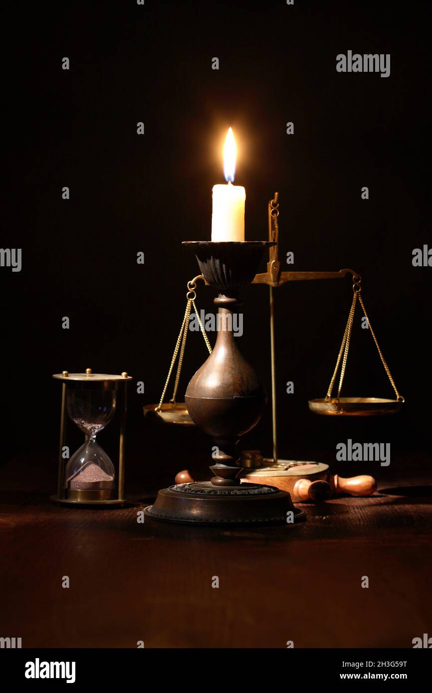 Elegant brass candlestick with lighting candle near hourglass and ...
