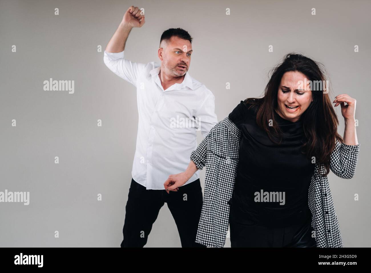 A man swings his hand at a battered woman standing on a gray background ...