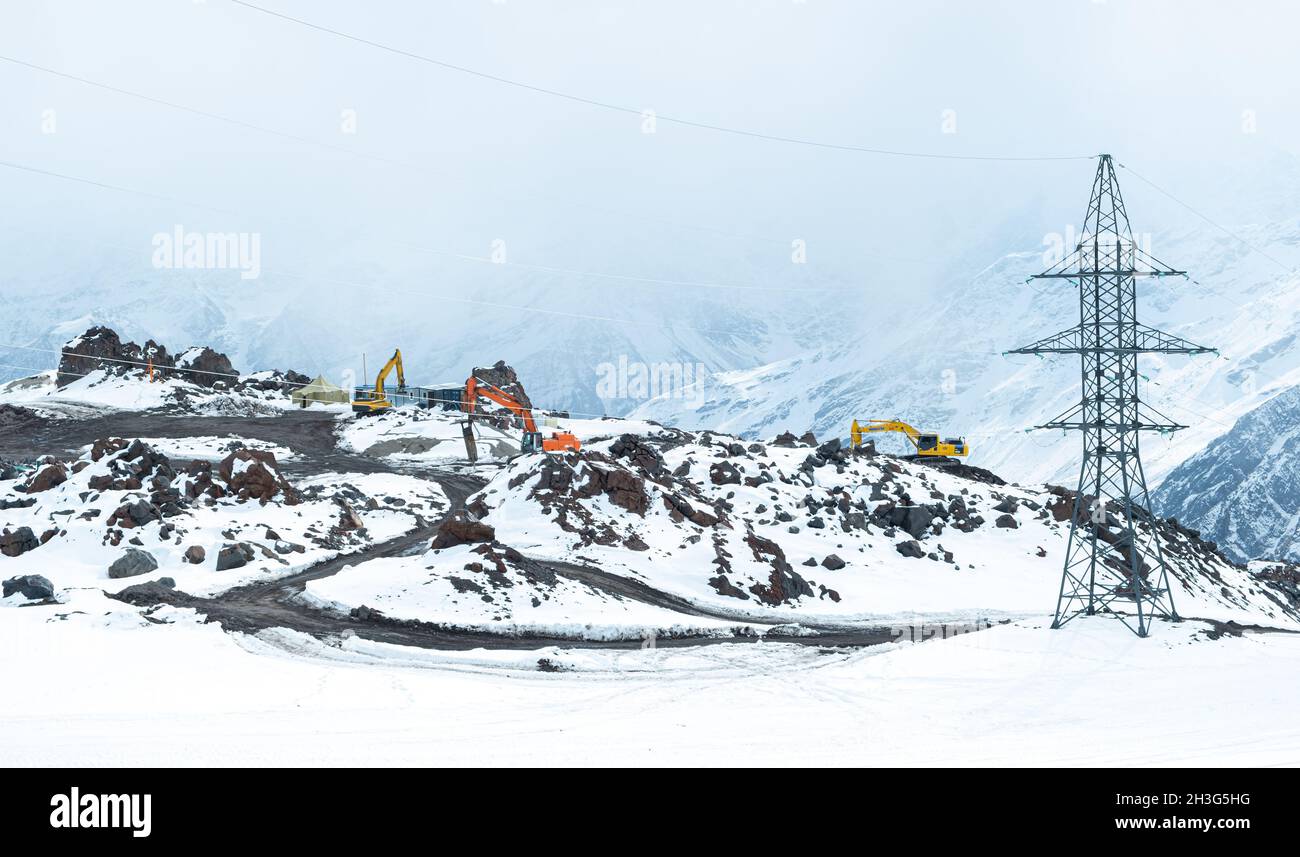 Three excavators are working in the snowy mountains next to the power ...