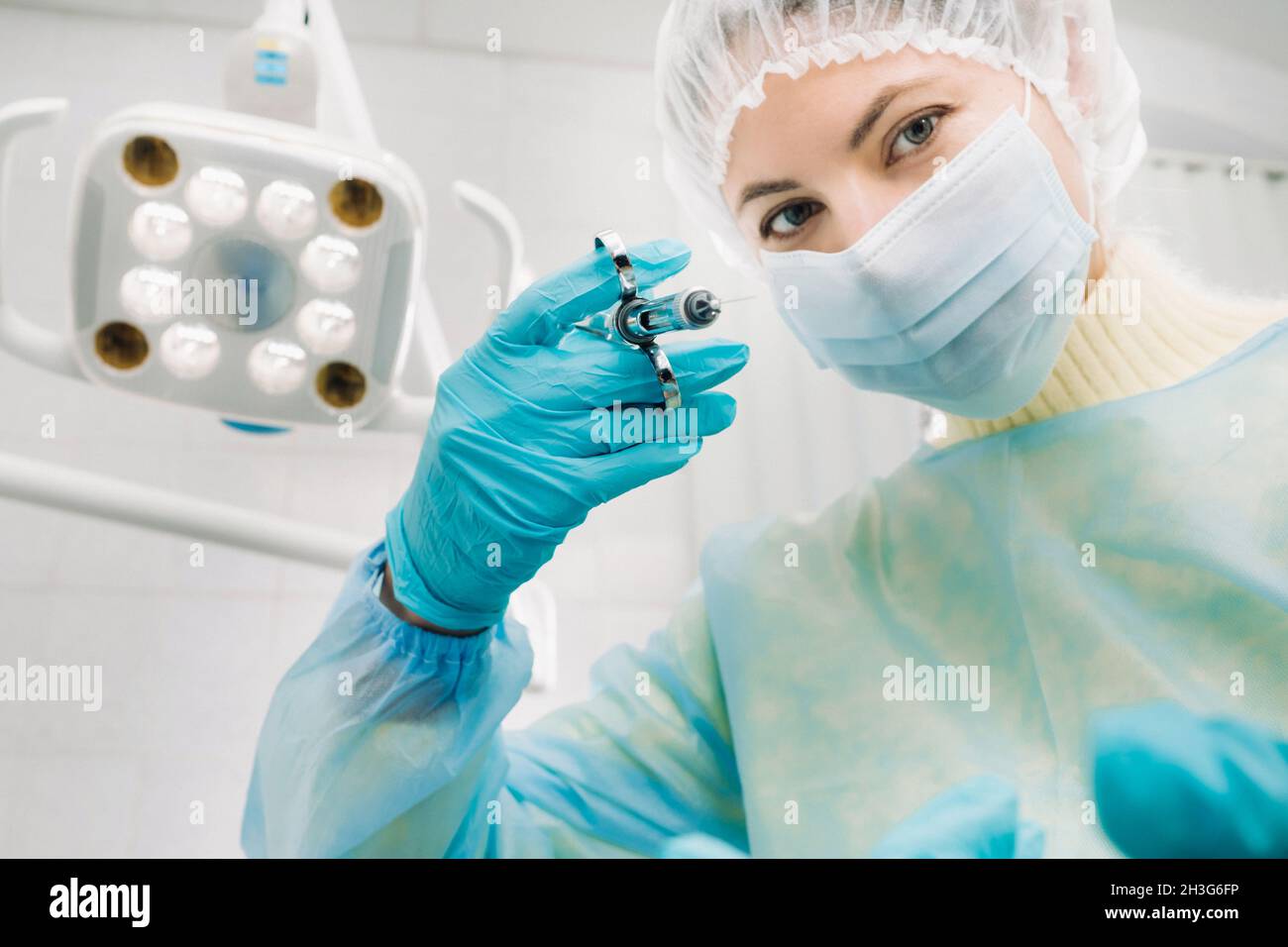 A masked dentist holds an injection syringe for a patient in the office ...