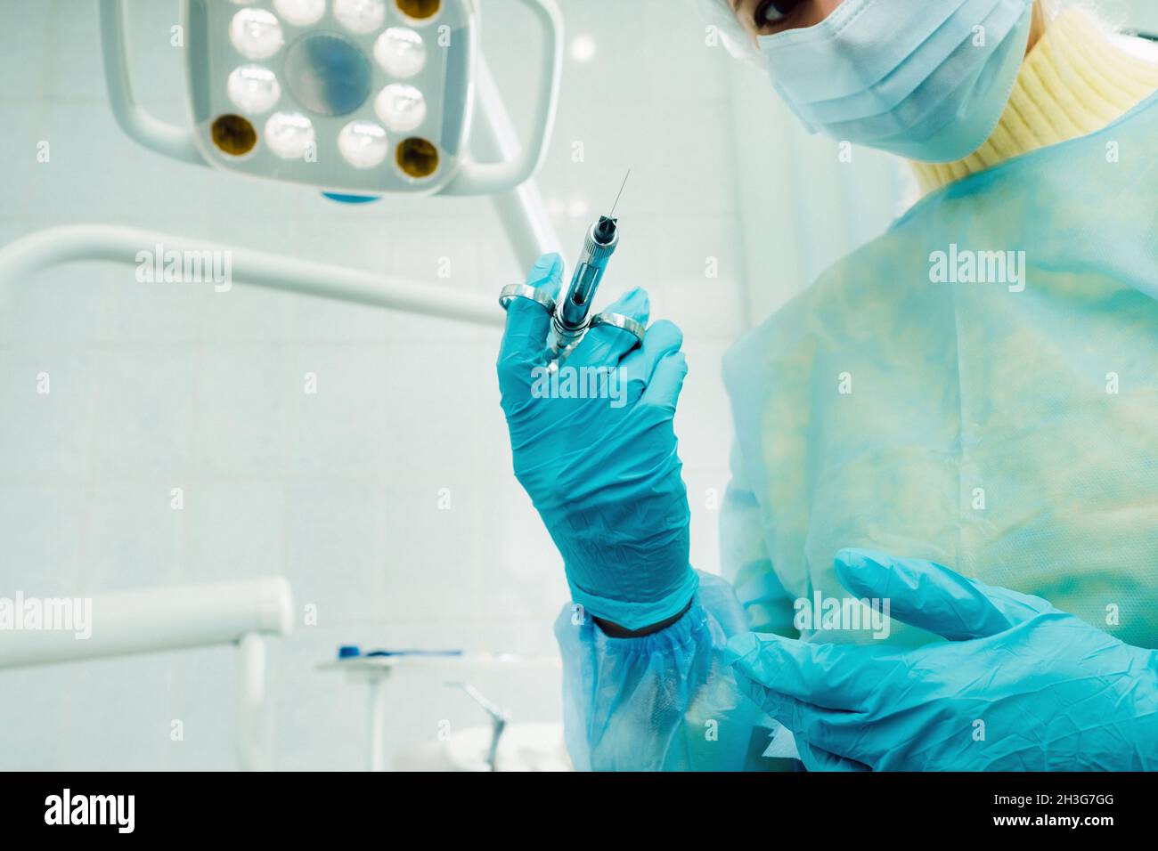A masked dentist holds an injection syringe for a patient in the office ...