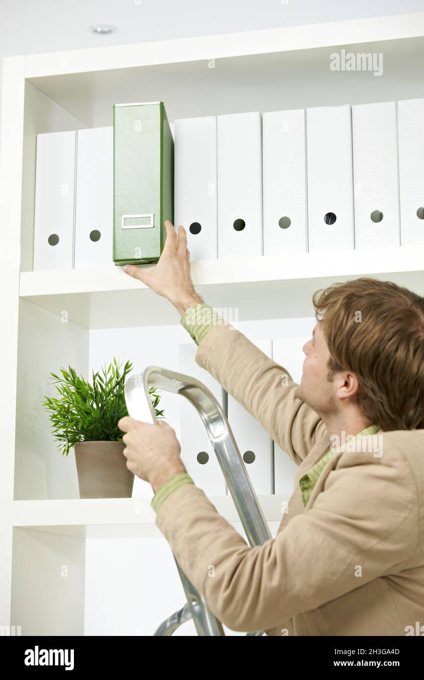 Businessman removing green folder from shelf Stock Photo - Alamy