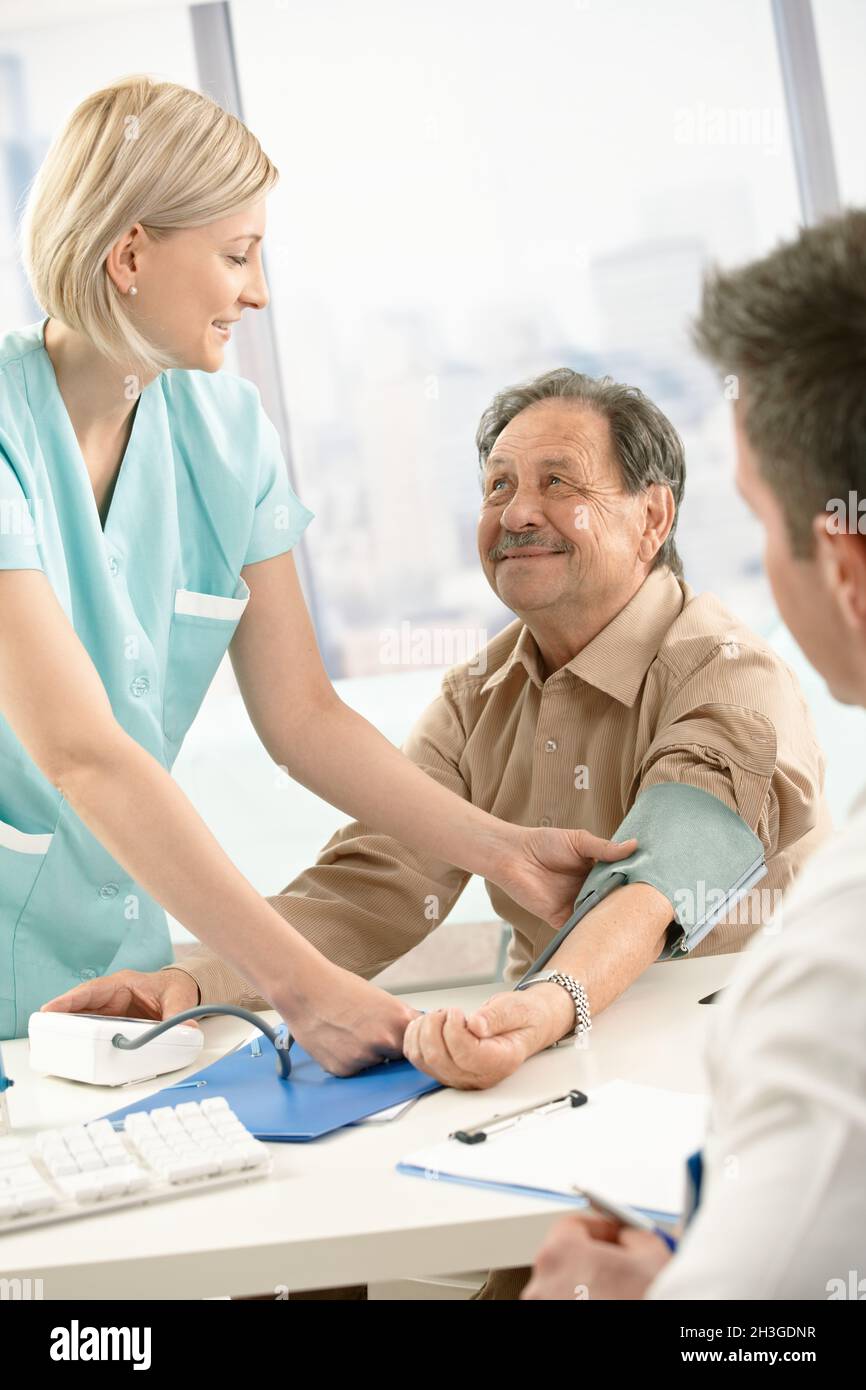 Smiling nurse measuring blood pressure of patient Stock Photo - Alamy