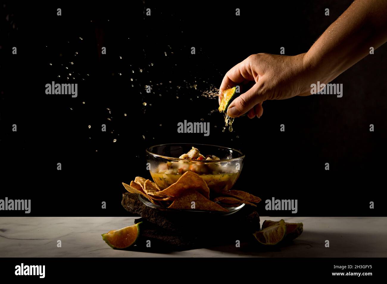 Hand squeezing a touch of lime onto a bowl of ceviche with tortilla ...