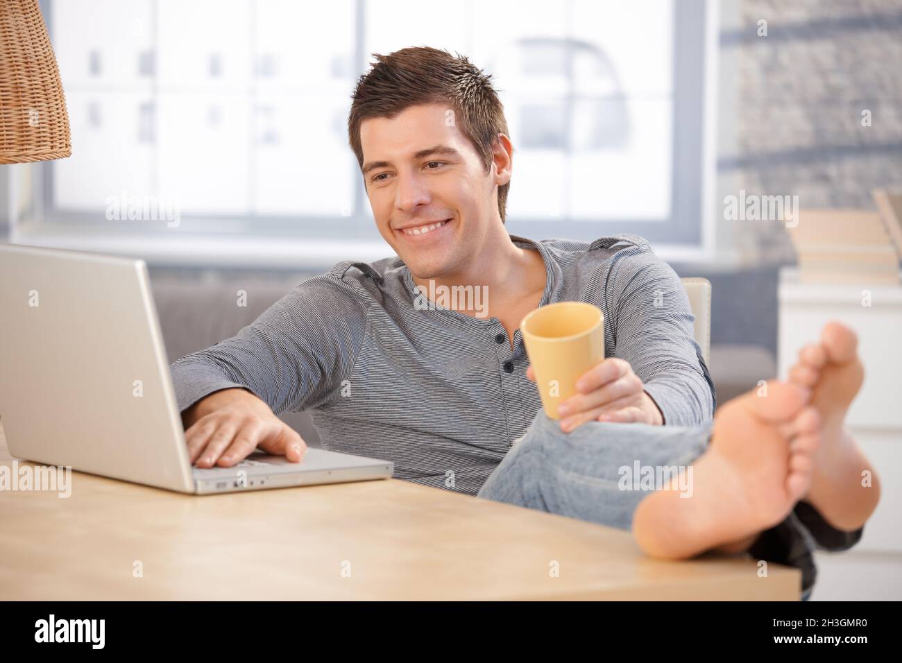 Laughing young man using computer at home Stock Photo - Alamy