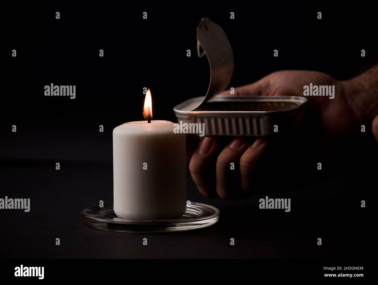 concept of energy blackout, lit candle, with can of preserves in man's ...