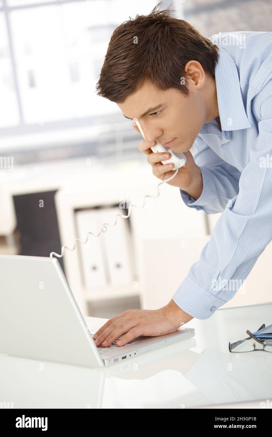 Young office worker on phone using computer Stock Photo - Alamy