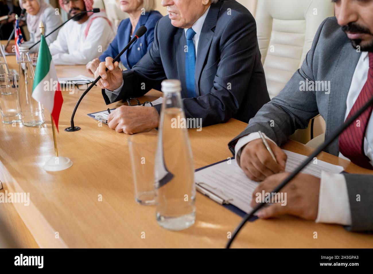Close-up of senior delegate in suit speaking into microphone while ...