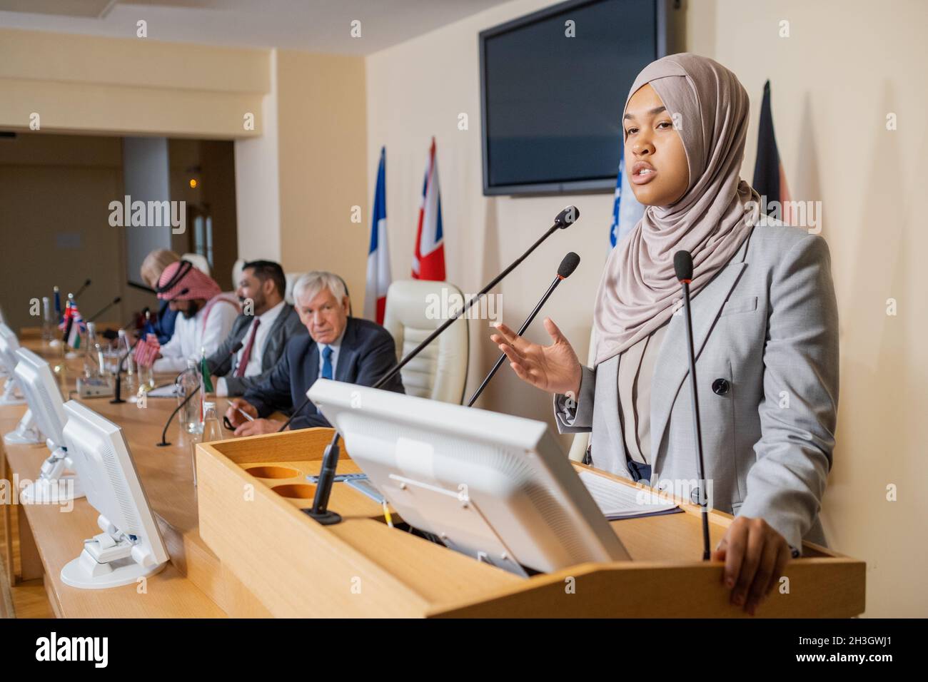 Confident young Muslim politician in hijab standing at rostrum and ...