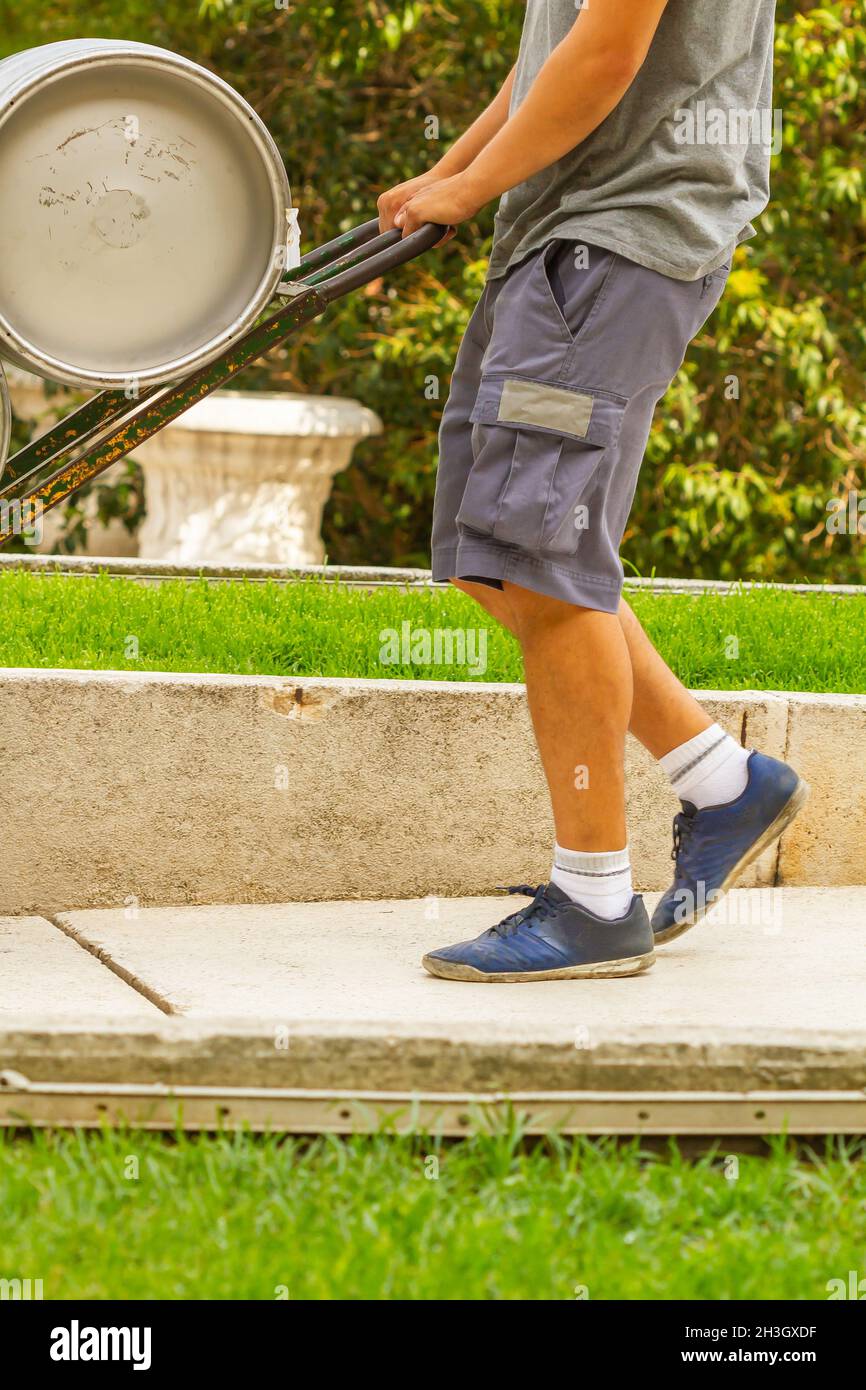 Vertical shot of a male worker pulling a wheelbarrow with a keg of beer ...