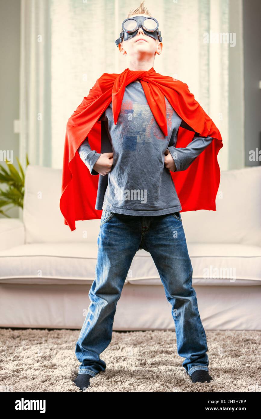 Proud young Super Hero posing in a red cape and goggles with hands on ...