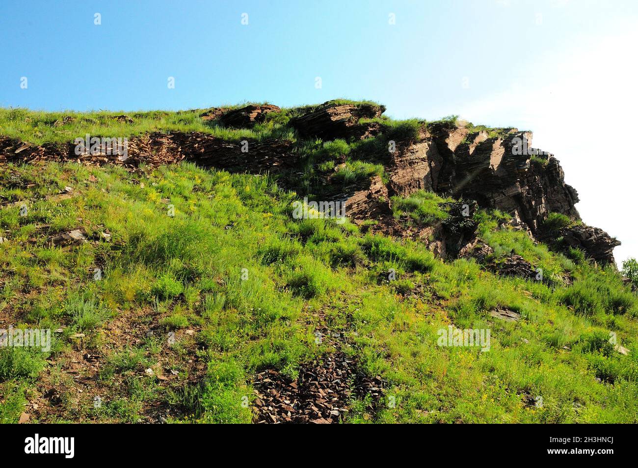 Flat layered stone formations on top of a mountain overgrown with low ...