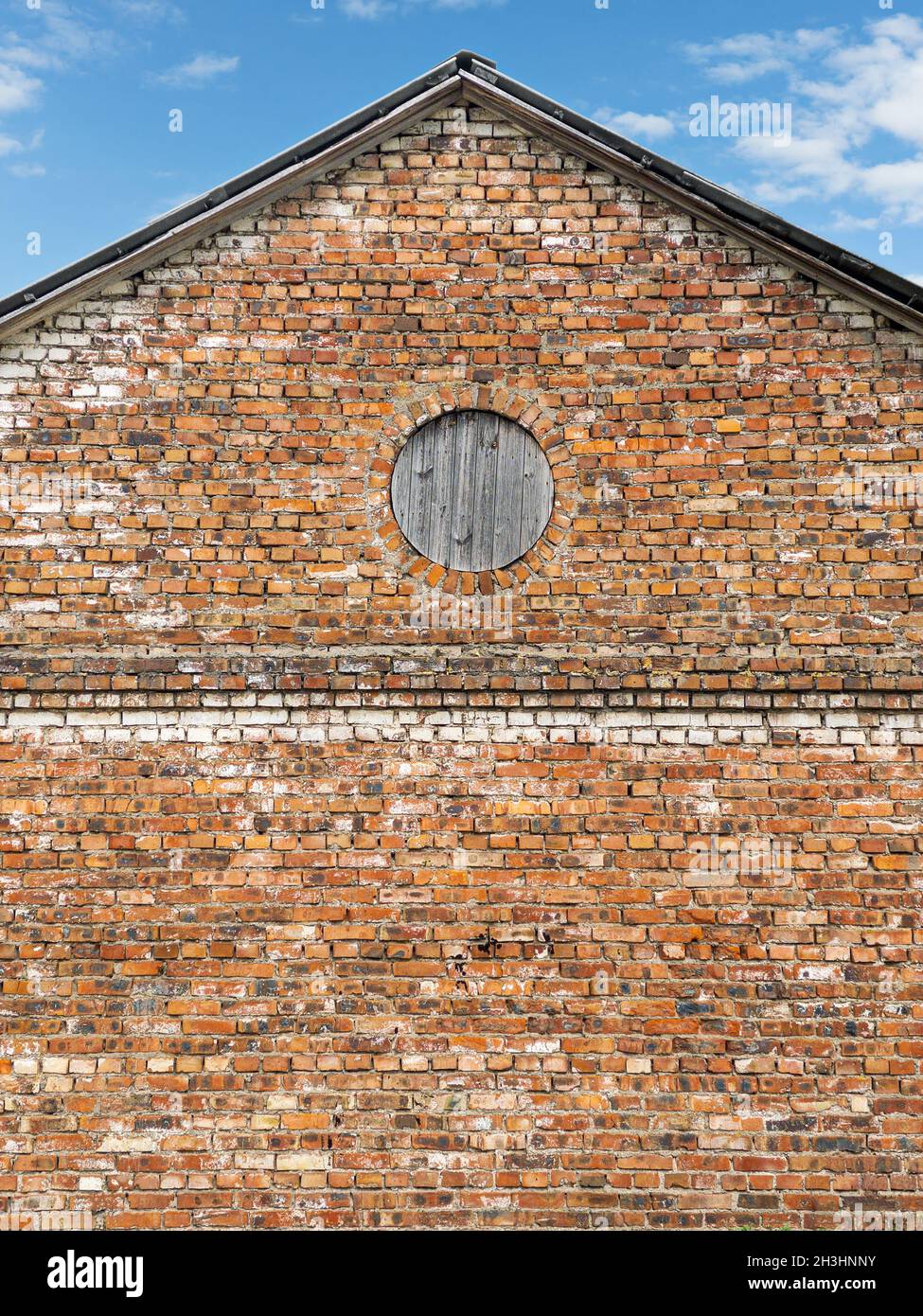 weathered red brick gable wall with boarded up round window. old ...