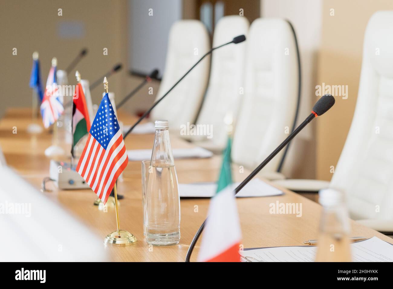 National flags placed on wooden conference table with microphones ...