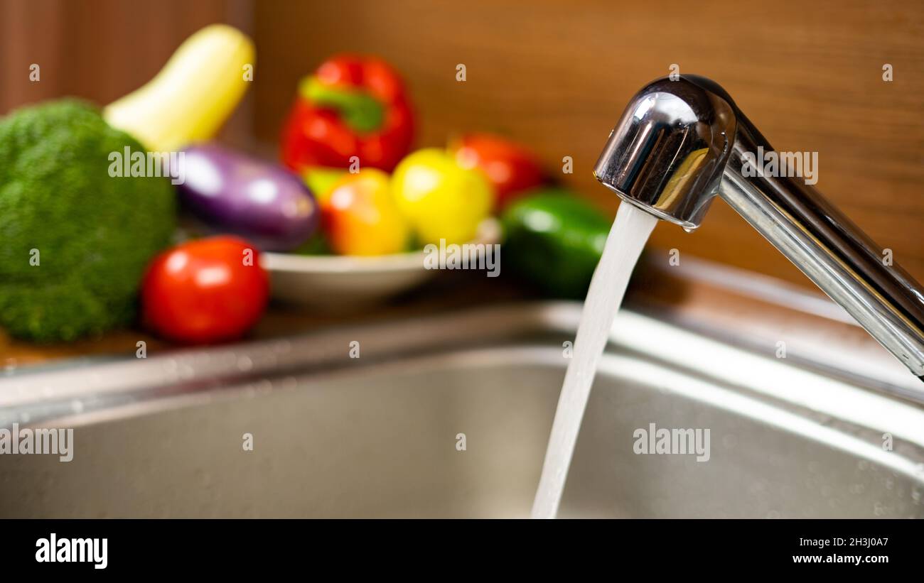 A stream of water from the tap on the background of vegetables. Close ...