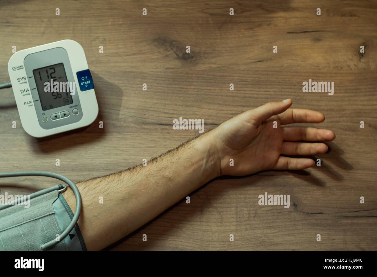 A man's hand and an automatic tonometer on a wooden table. On the ...