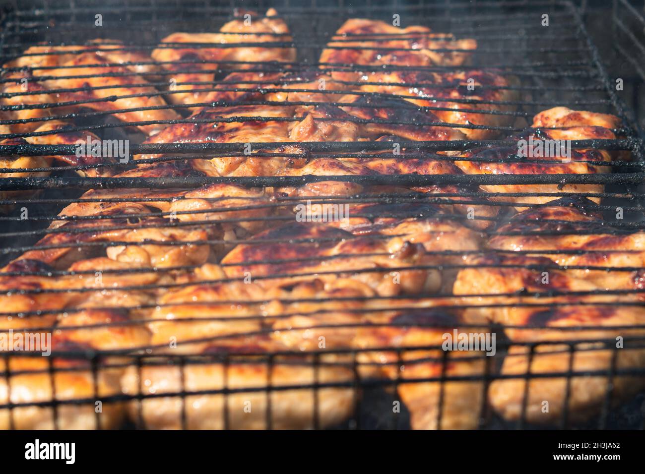 Fried chicken wings with a golden crust lay on a black, greasy grate on ...