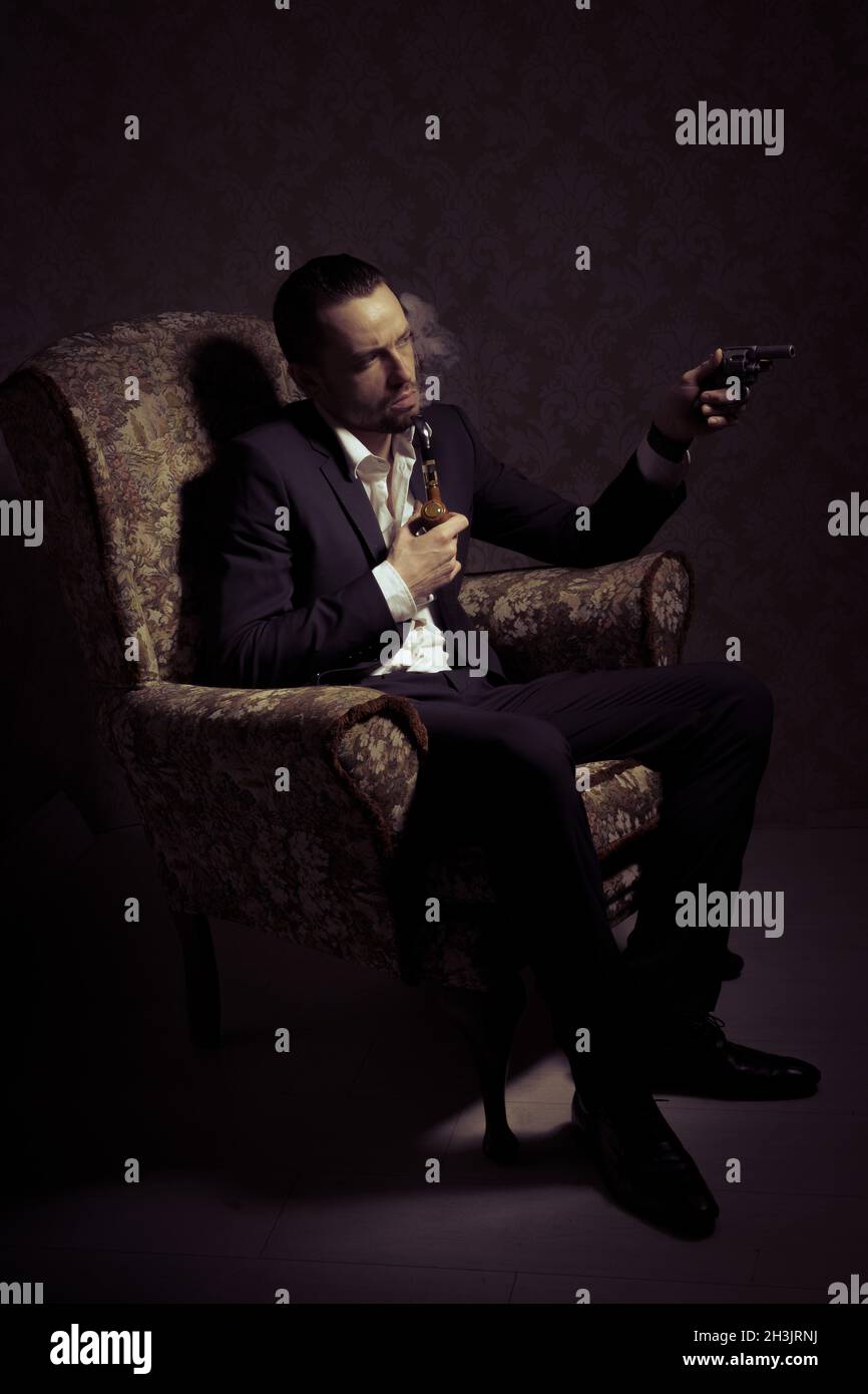 Young handsome man sitting in chair, holding gun and smoking pipe over ...