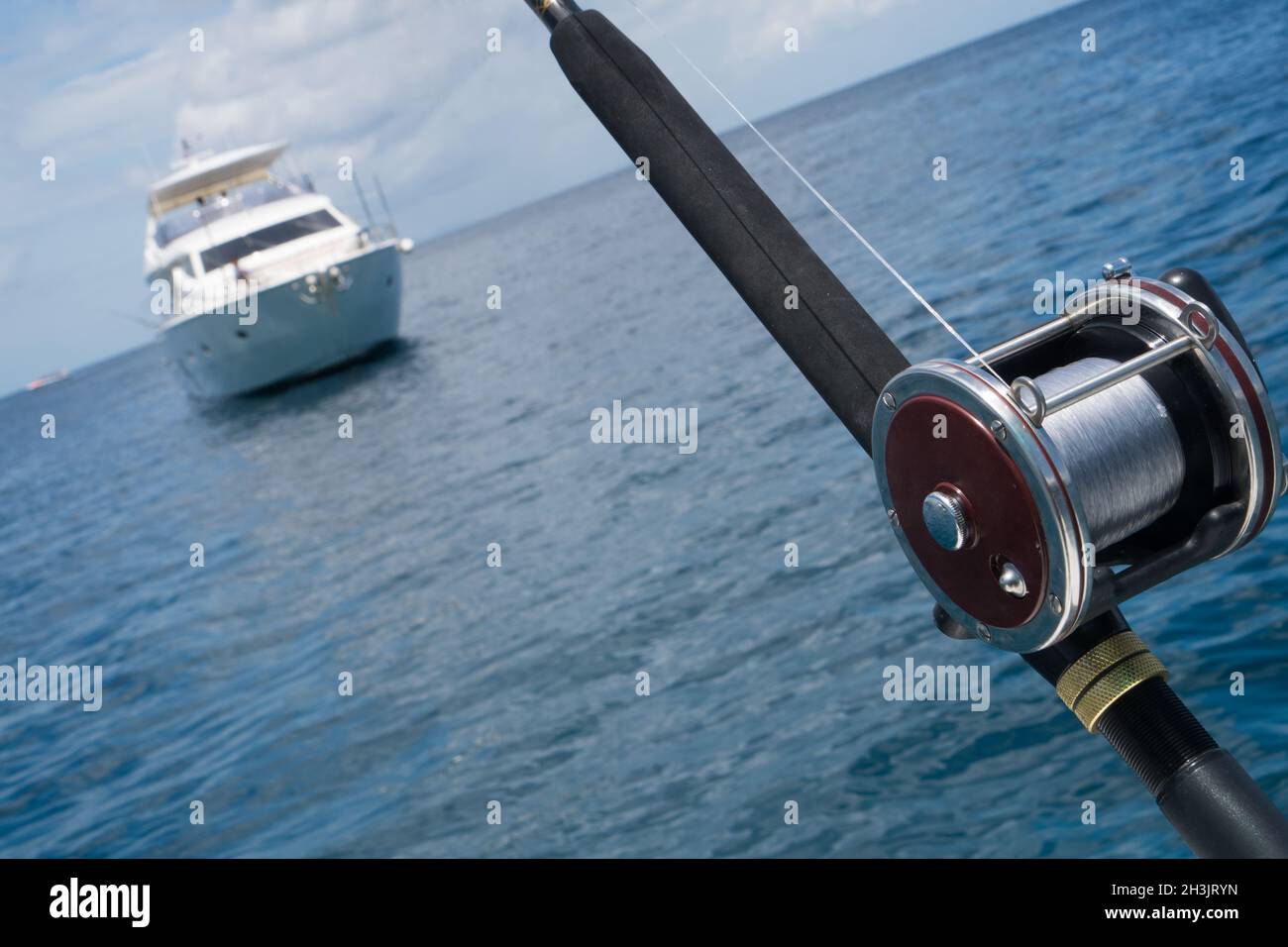 Fishing rod on a boat over blue sky and white sailing boat in the sea ...