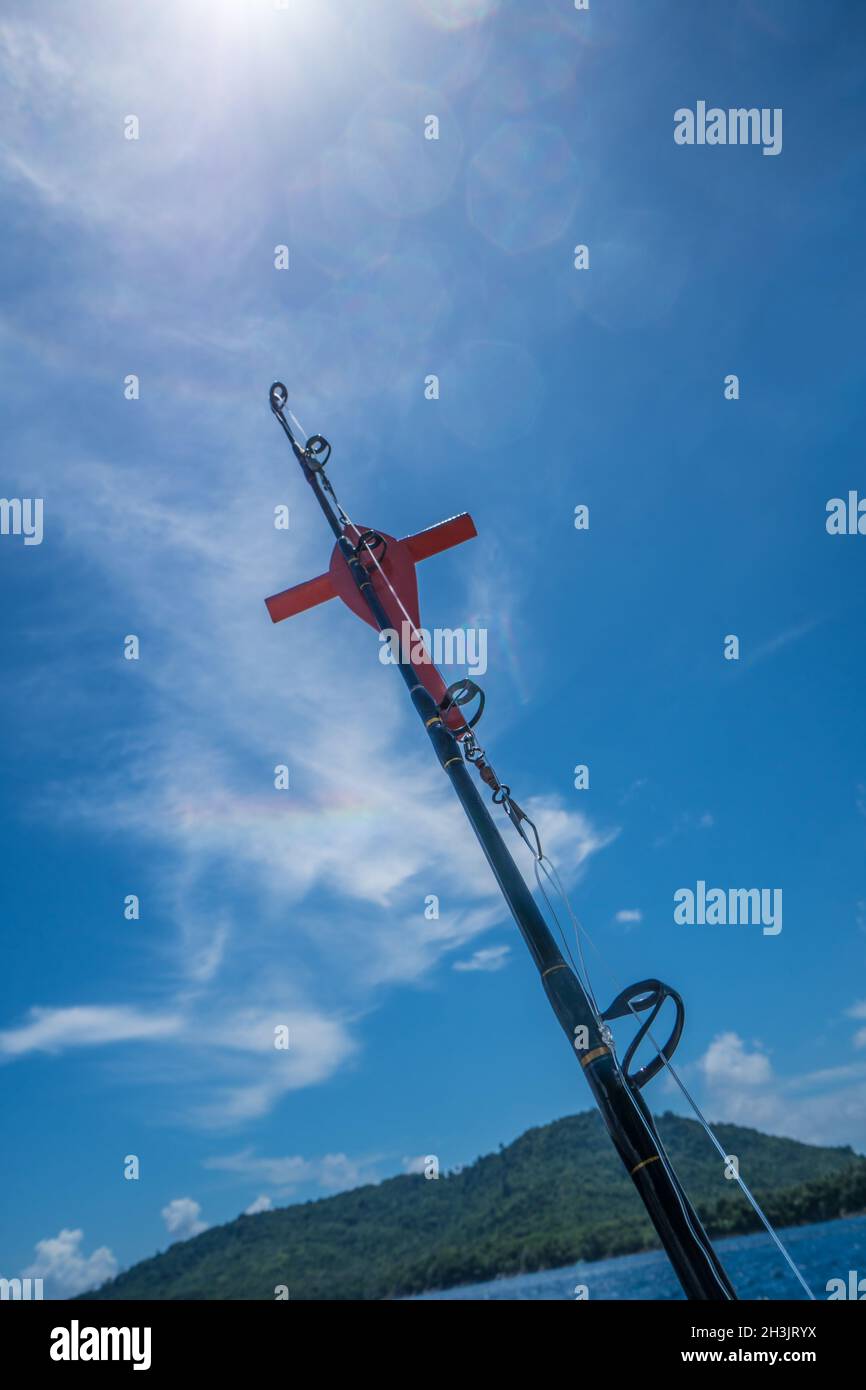 Top of the fishing rod on a boat over blue sky and green island ...