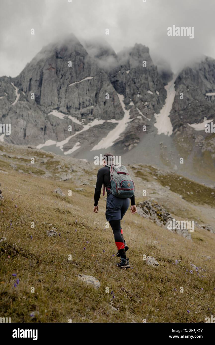 Back view of a young caucasian male hiker walking up the grassy ...