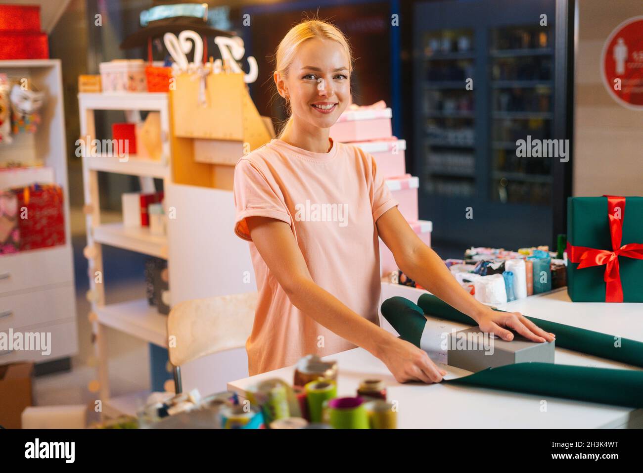 Attractive young woman wrapping festive Christmas gift box in craft ...