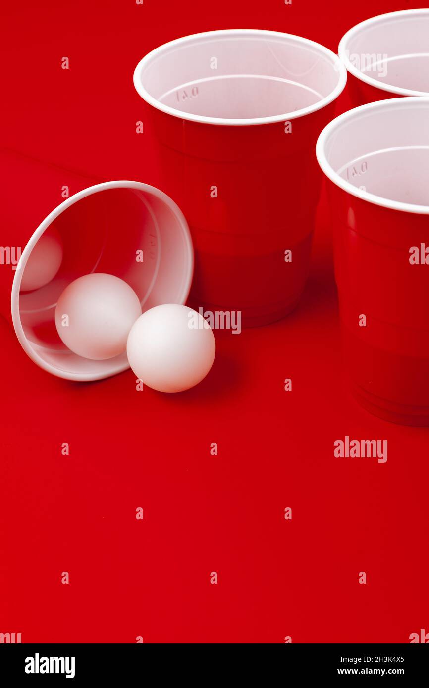Cups and plastic ball on red background. Beer pong game Stock Photo - Alamy