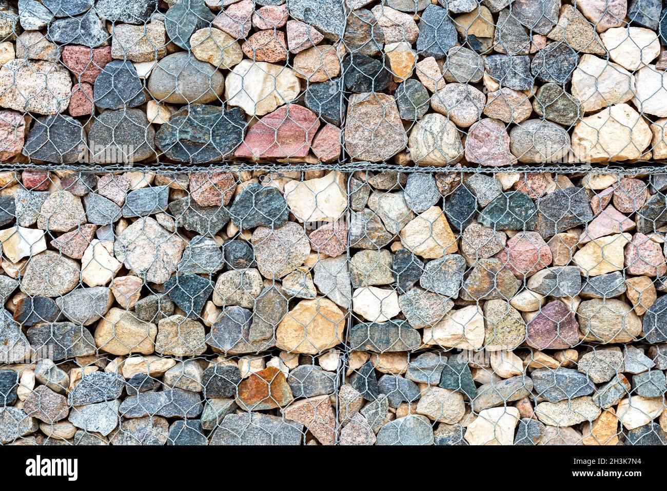 Stone wall with metal grid and rough stones as background. Rock texture ...