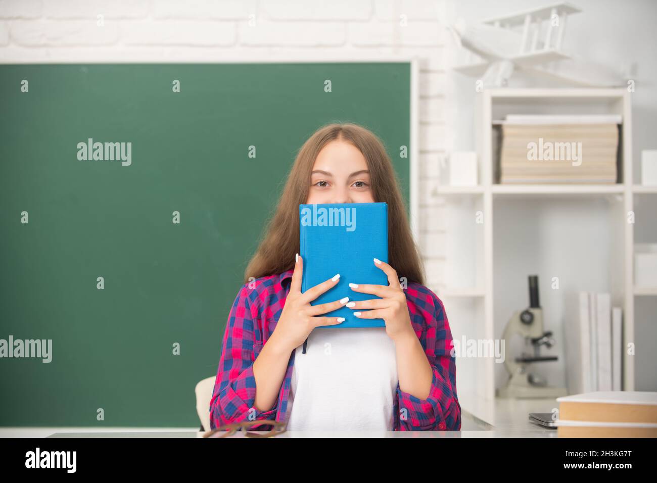 child hiding behind book at school on blackboard background, knowledge ...