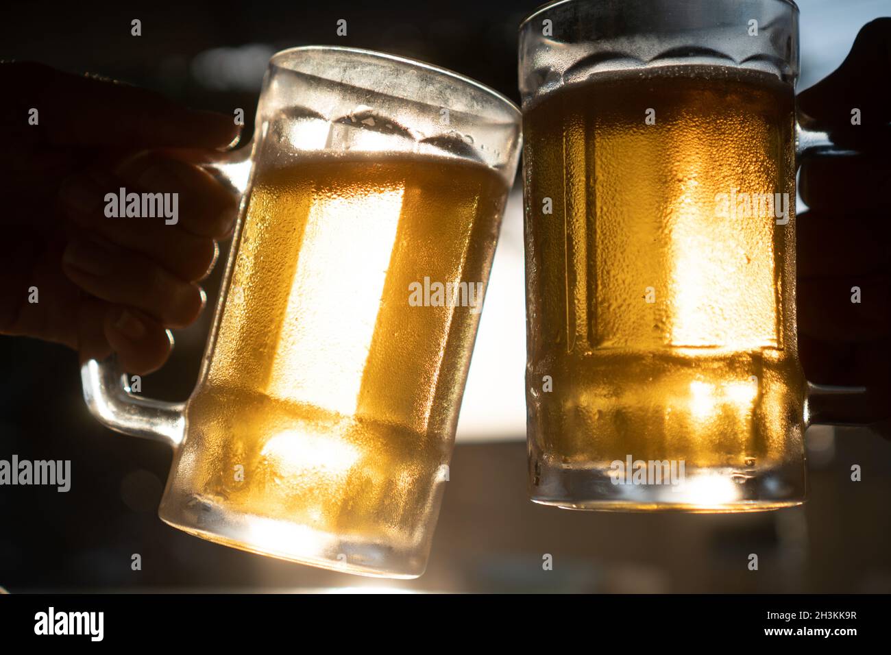 Closeup toast clinking fresh lager beer mugs with sun rays in hot ...