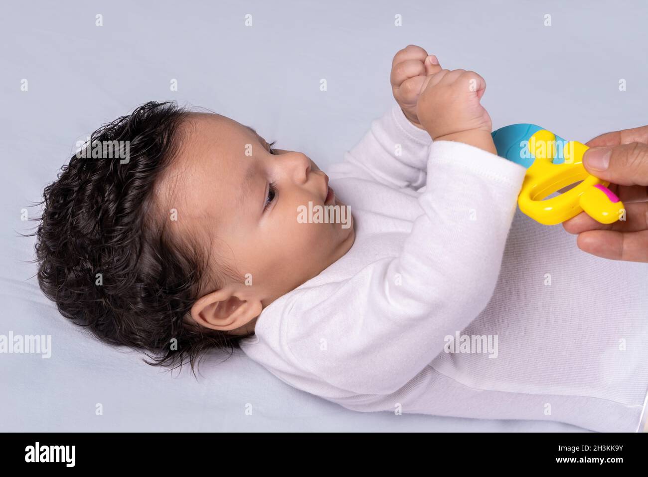 Infant lying on his back with his hands up trying to grab a toy Stock ...
